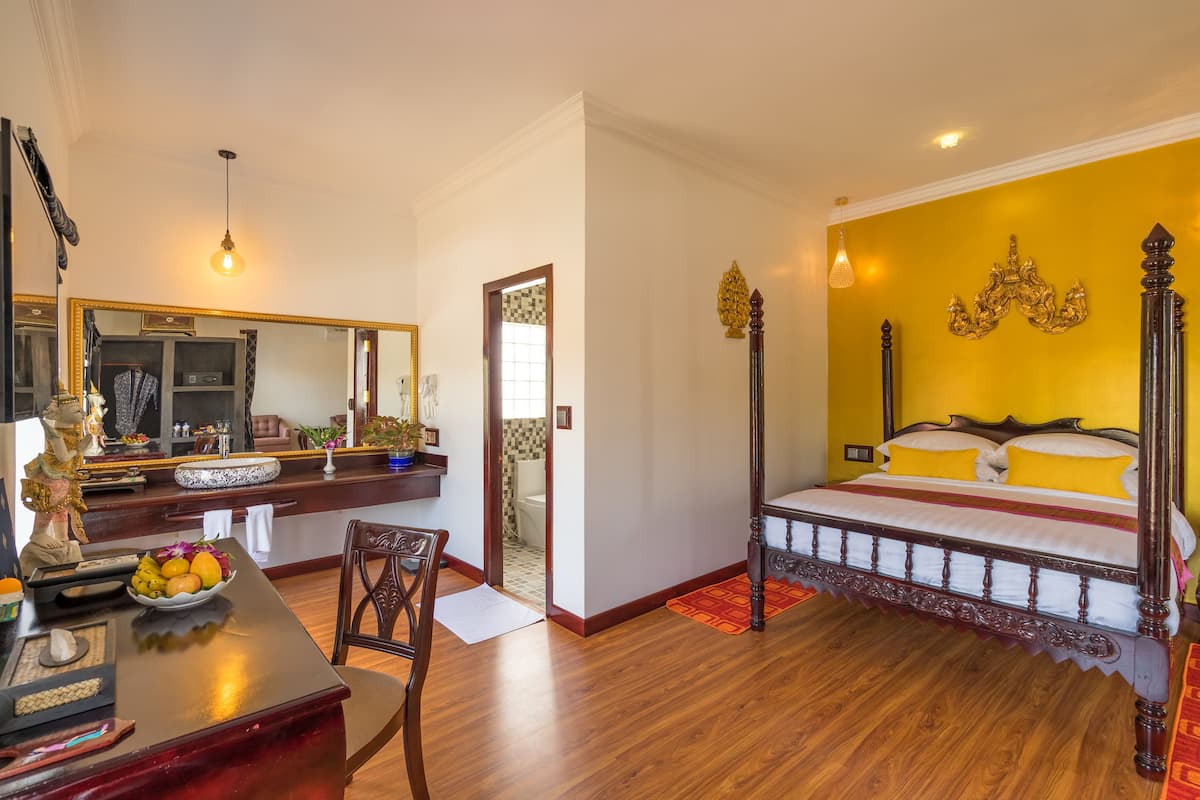 Quarto com uma cama grande, piso de madeira, escrivaninha com espelho e uma fruteira.