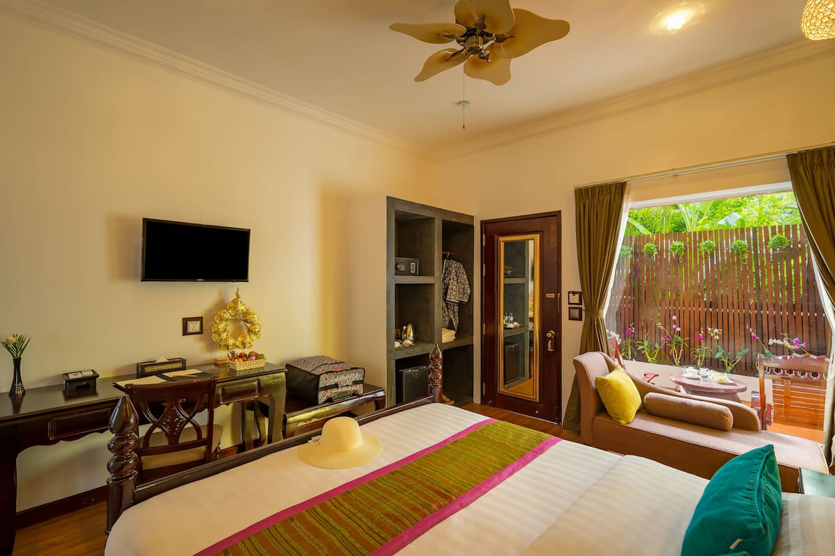 Quarto de hotel com cama, escrivaninha, televisão e varanda com vista para o verde.