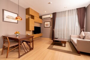 Uma sala de estar moderna com uma mesa de jantar de madeira, um sofá e uma televisão. Há um aparelho de ar condicionado na parede e um quadro emoldurado acima da televisão.