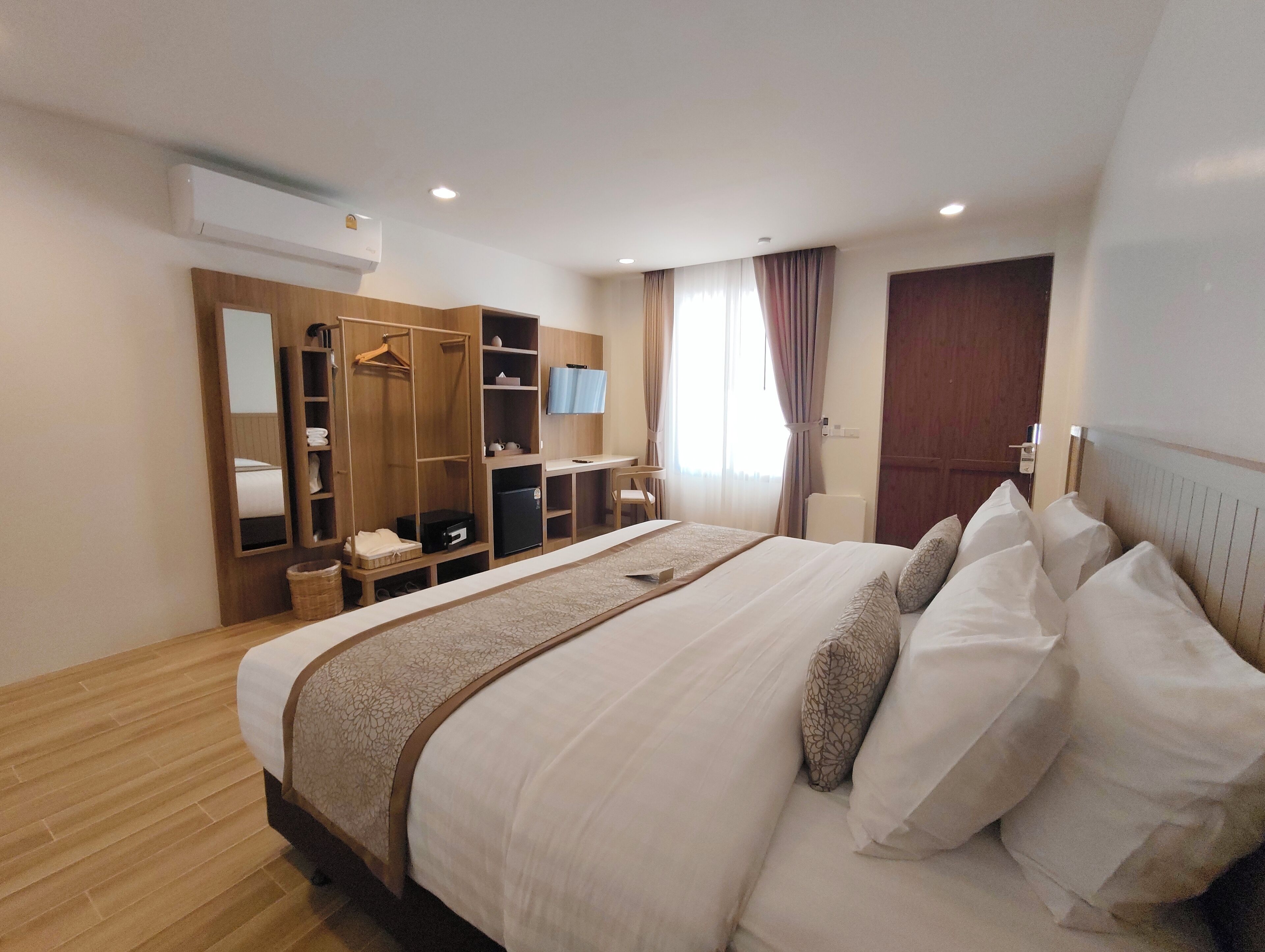 Quarto de hotel com uma cama grande, um guarda-roupa, uma escrivaninha e uma televisão.