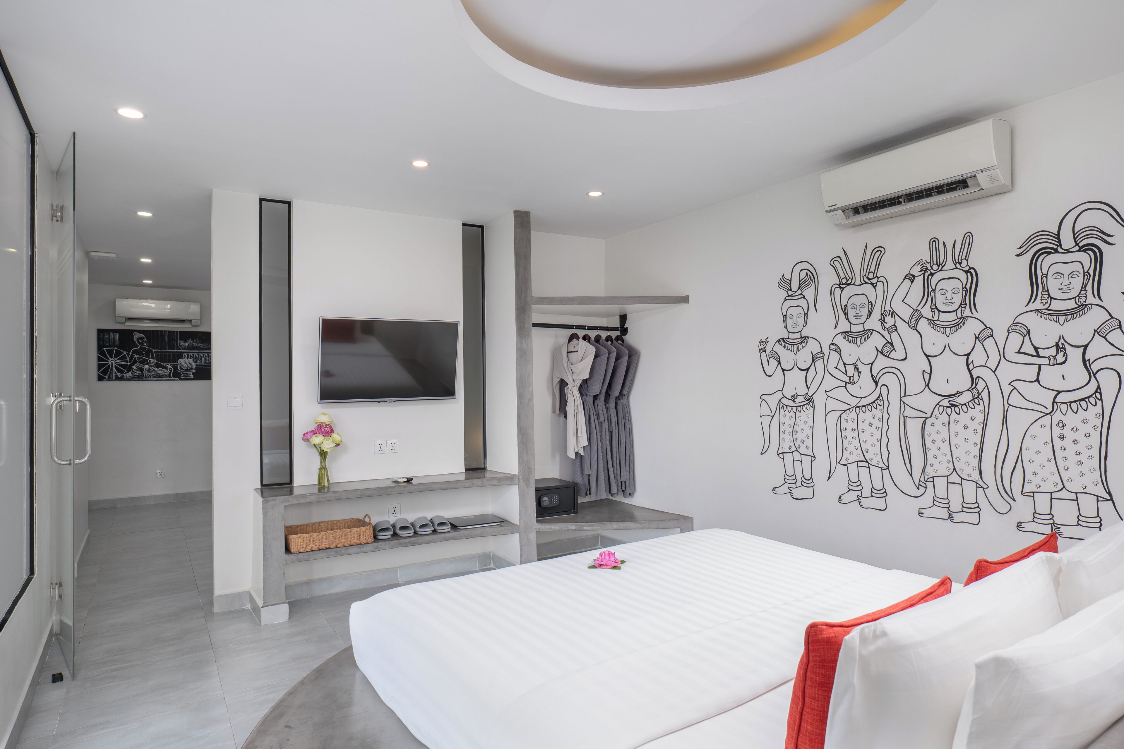 Quarto de hotel moderno com uma cama grande, televisão de tela plana, ar-condicionado fixado na parede e um mural decorativo.