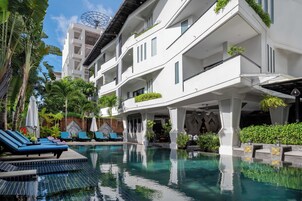 Um hotel moderno com área de piscina, espreguiçadeiras e vegetação.