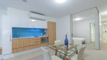 Uma cozinha moderna com armários brancos, painel de fundo azul e uma mesa de jantar de vidro com cadeiras brancas.