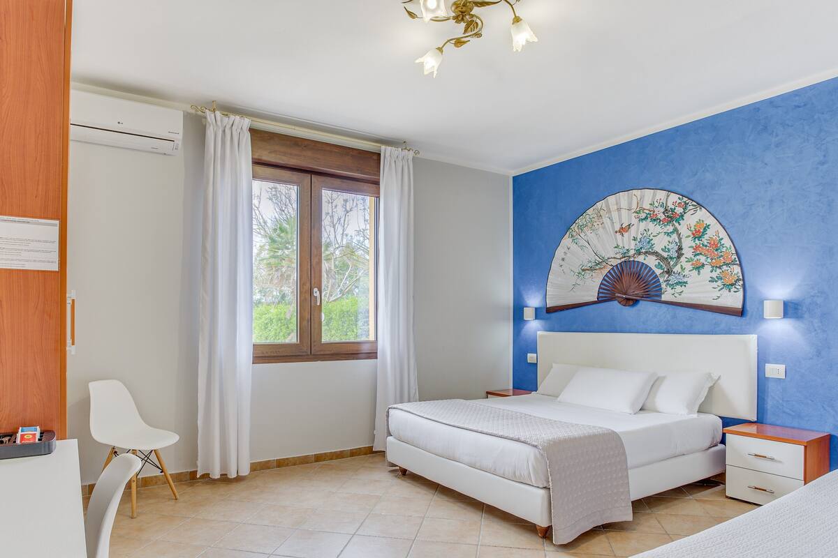 Quarto com cama, mesas de cabeceira, escrivaninha e uma cadeira.