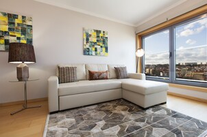 Uma sala de estar moderna com um sofá seccional, um tapete estampado e grandes janelas com vista para a cidade.