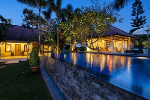 Piscina com deck revestido, rodeada por um gramado bem cuidado e palmeiras.