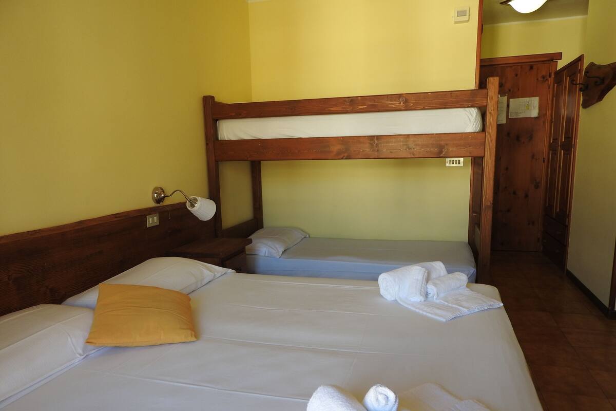 Quarto com duas camas de solteiro, cabeceira de madeira, mesa de cabeceira com abajur e travesseiro amarelo.