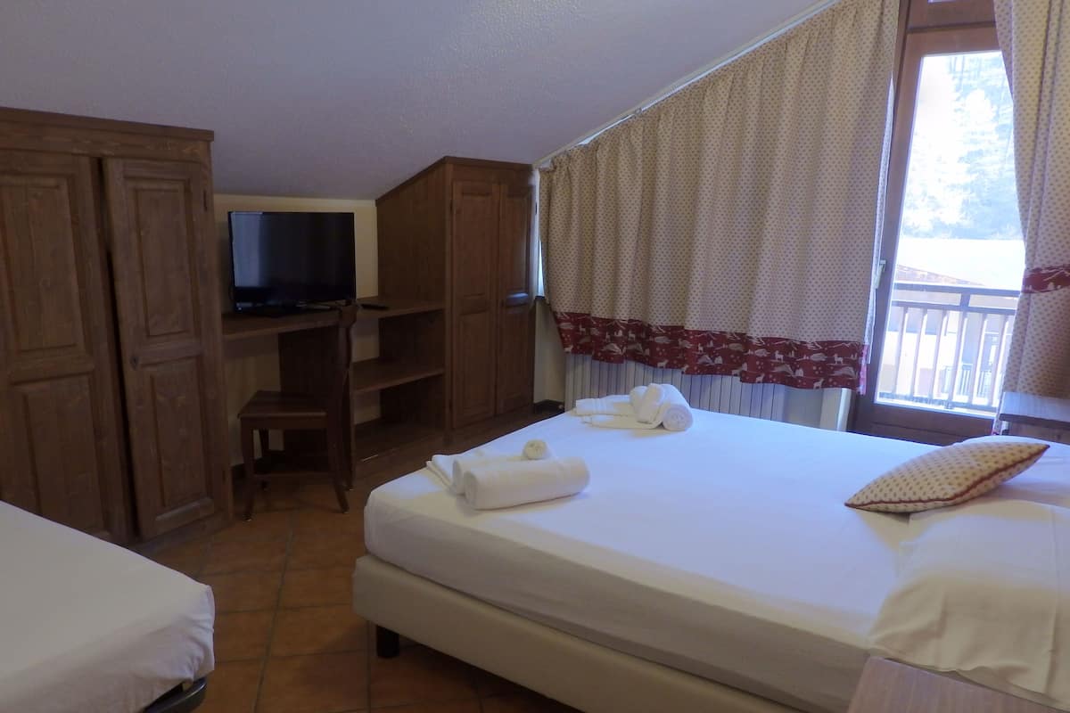 Quarto de hotel com cama, televisão, armários de madeira e varanda com cortinas.