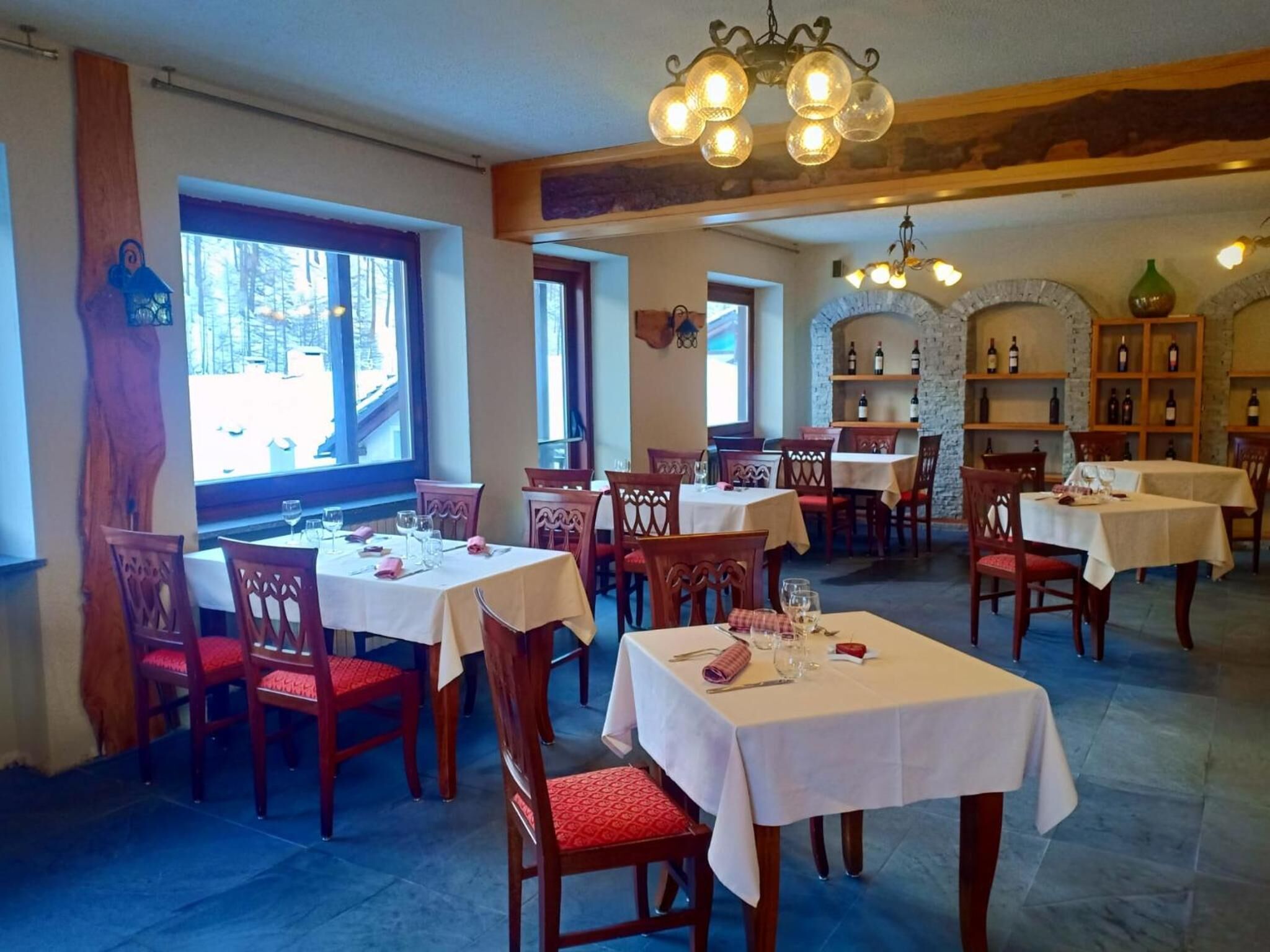 Restaurante com várias mesas e cadeiras, um candelabro e garrafas de vinho em prateleiras.