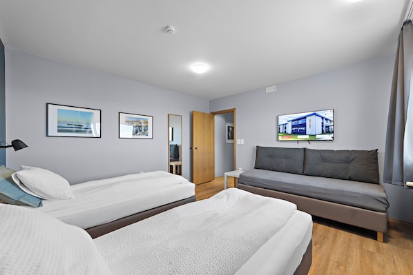 Quarto de hotel com duas camas de solteiro, um sofá, uma TV e quadros nas paredes.