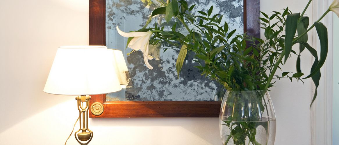 Um abajur com cúpula branca e um vaso transparente com plantas verdes e flores brancas.