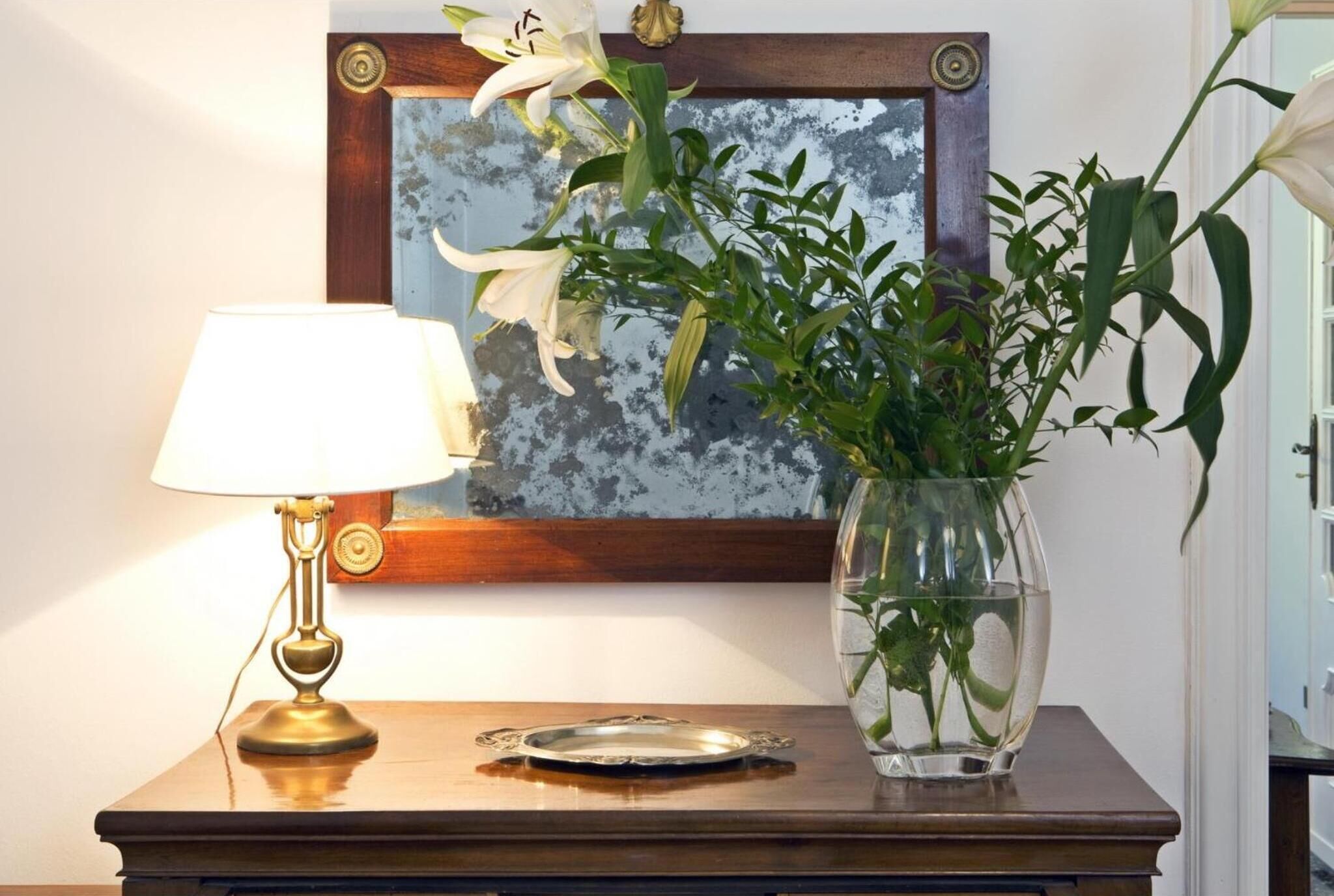 Uma mesa com uma lâmpada, um vaso com plantas e um espelho decorativo.
