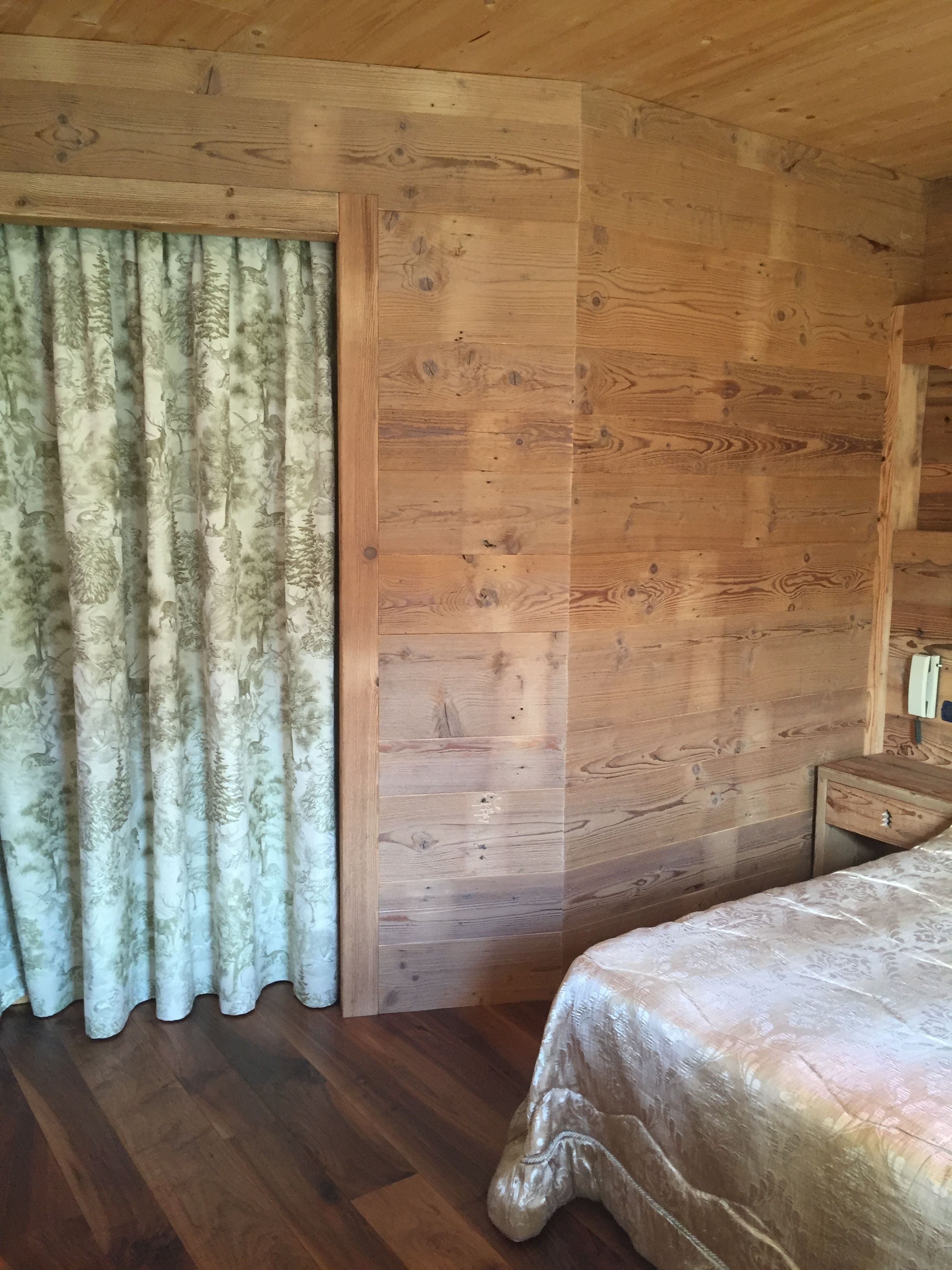 Quarto de cabana de madeira com cama, mesa de cabeceira e janela com cortinas.