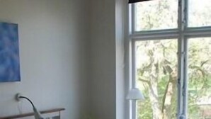 Quarto com cama, janela com vista para vegetação, radiador e luminária.