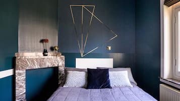 Quarto com lareira de mármore, uma obra de arte geométrica na parede e uma cama com duas almofadas.