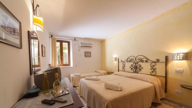 Quarto de hotel com duas camas, uma escrivaninha com luminária, uma janela e ar-condicionado fixado na parede.