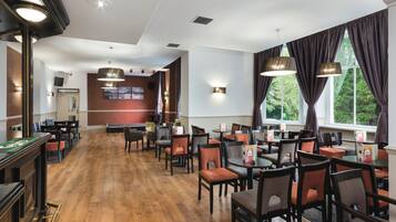 Uma sala de jantar ampla com piso de madeira, várias mesas e cadeiras.