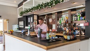 Uma área de bar com um bartender, diversas garrafas de bebidas alcoólicas e um balcão de bar bem abastecido.