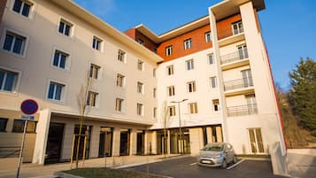 Um hotel de vários andares com design moderno, apresentando área de estacionamento e céu claro.