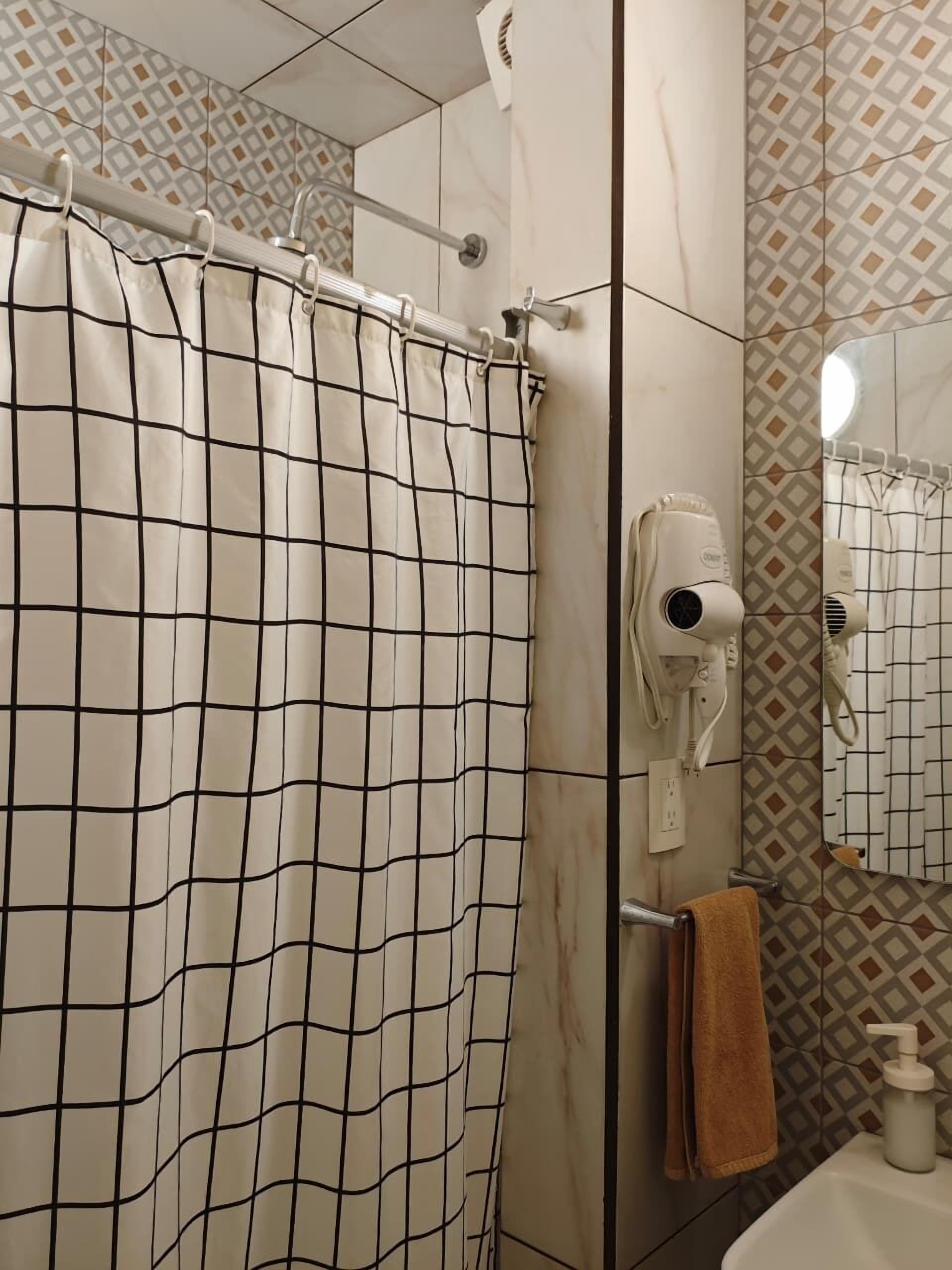 Casa de banho com cortina de chuveiro padronizada, secador de cabelo, porta-toalhas e espelho.