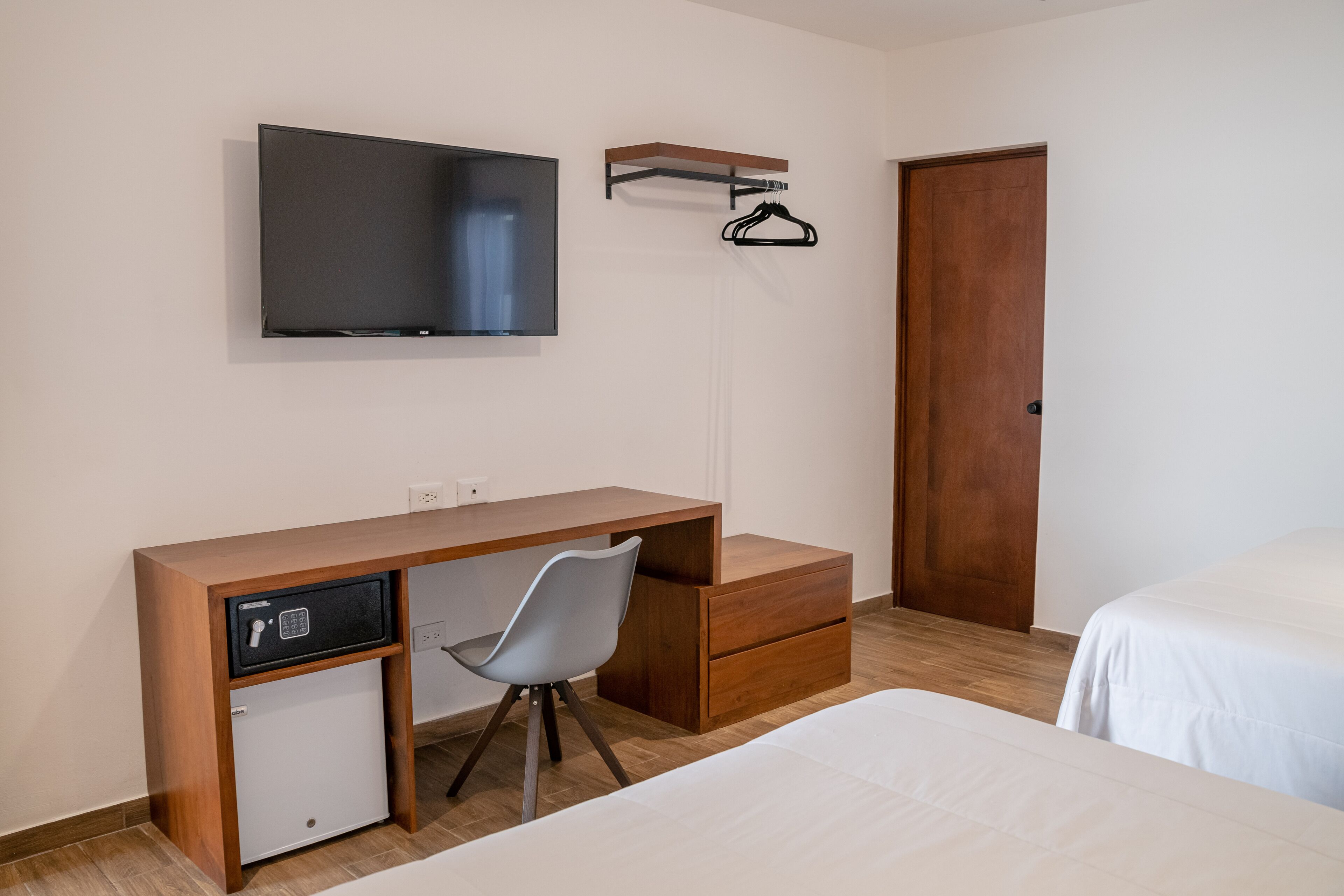 Quarto com escrivaninha de madeira, uma cadeira, televisão, guarda-roupa e cama.