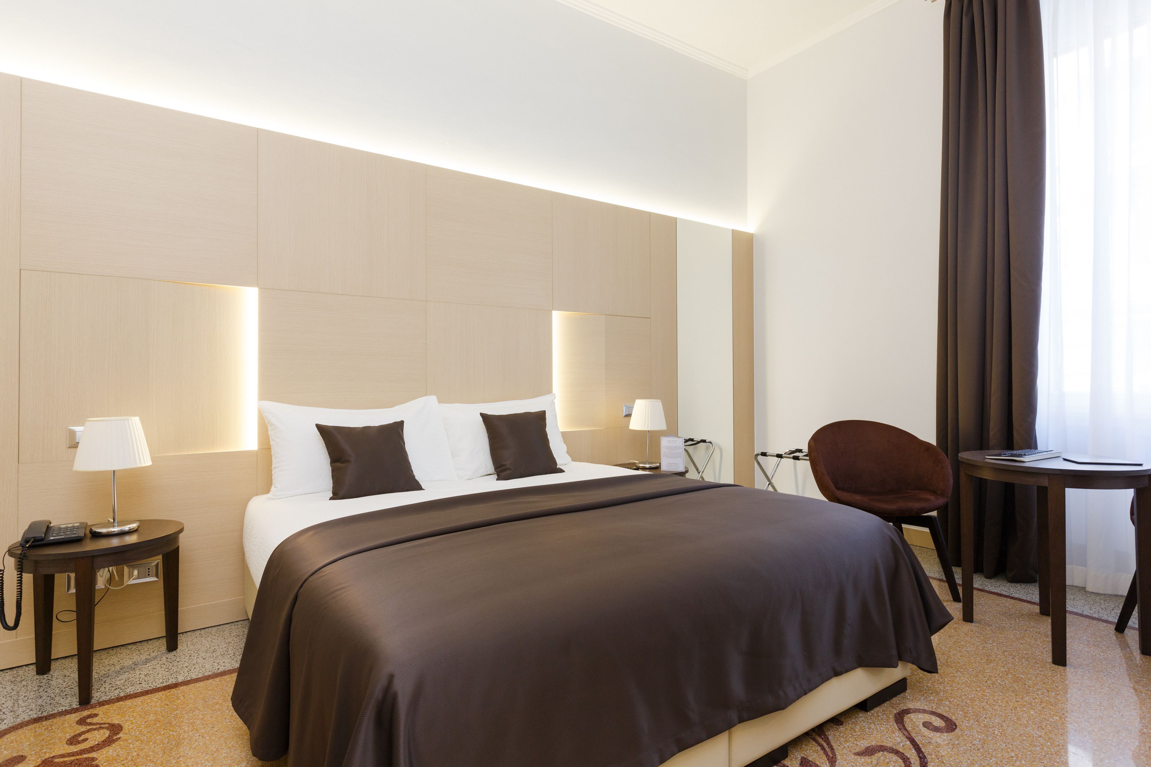 Quarto de hotel com uma cama grande, mesas de cabeceira, escrivaninha e uma cadeira.