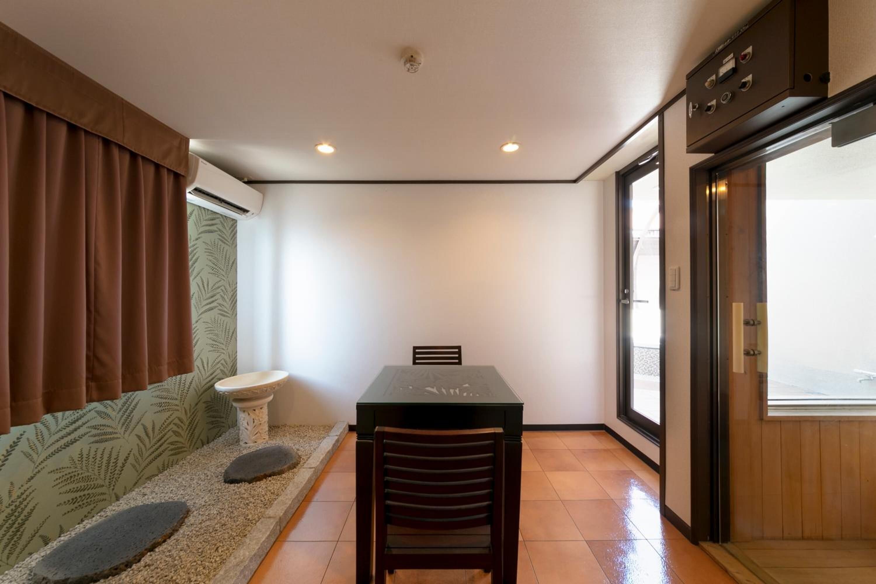 Quarto compacto com mesa de jantar, um banquinho, um arranjo decorativo de pedras e uma porta deslizante que dá para uma varanda.