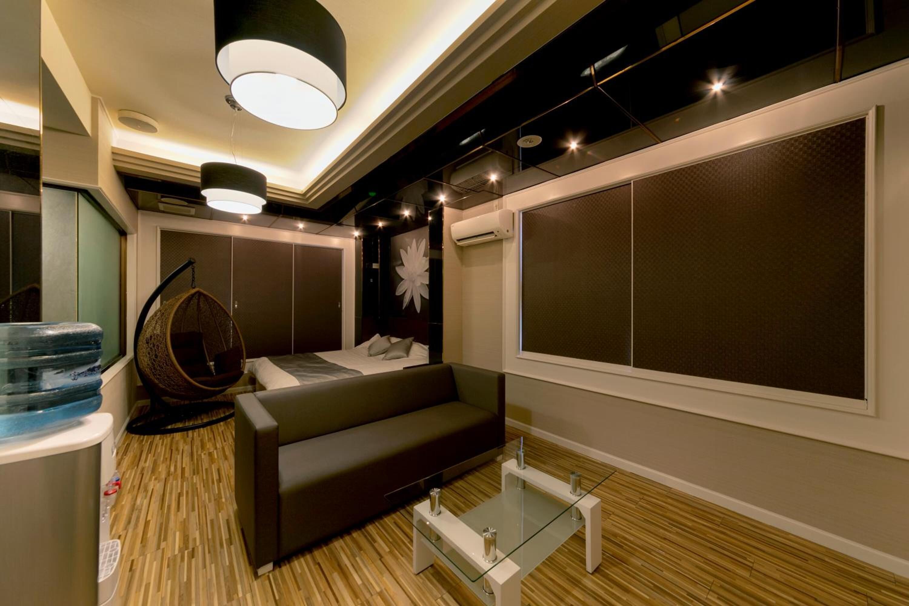 Quarto moderno com sofá marrom escuro, mesa de centro de vidro, cadeira suspensa e uma janela grande com persianas.