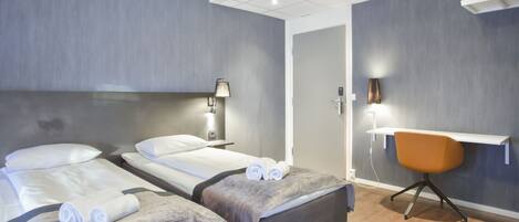 Quarto de hotel moderno com duas camas de solteiro, uma mesa e uma cadeira.