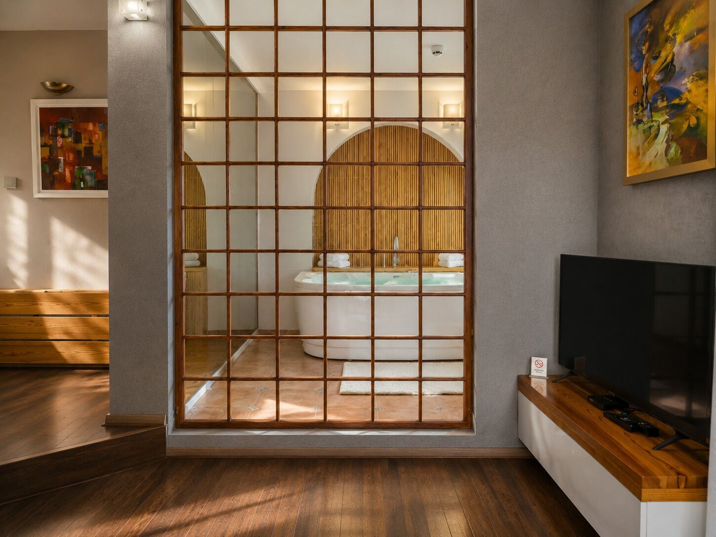 Quarto moderno com porta de correr em madeira, banheira, televisão e um quadro na parede.