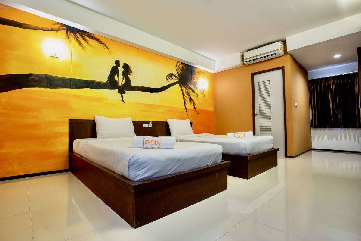 Quarto de hotel com duas camas, um mural retratando um casal num balanço e um aparelho de ar condicionado sobre a porta.