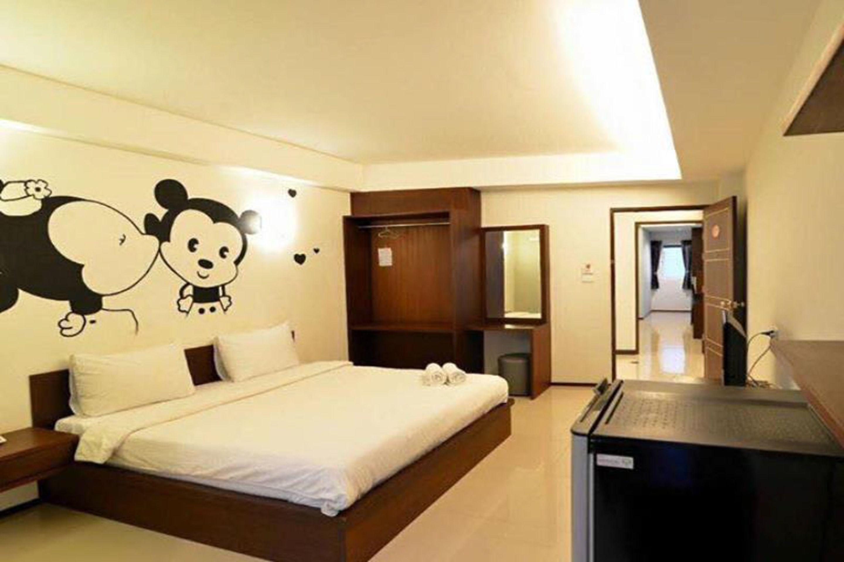 Quarto de hotel com cama, escrivaninha, televisão e parede com personagens de desenho animado.