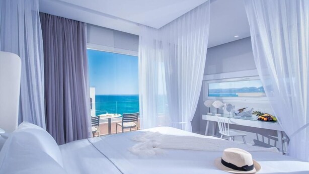 Quarto de hotel com uma cama grande, uma mesa de jantar e vista para o oceano.
