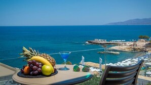 Uma mesa com frutas e uma bebida, com vista para a costa, edifícios e o mar.