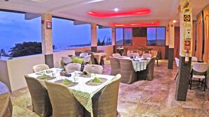 Restaurante com mesas preparadas para refeições, um extintor de incêndio e vista para o oceano.