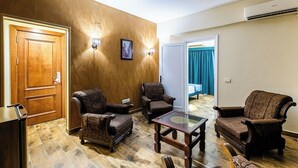 Uma sala de estar com uma porta de madeira, dois poltronas, uma mesa de centro de vidro e um aparelho de ar condicionado na parede.