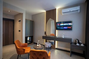 Quarto de hotel moderno com televisão de tela plana, escrivaninha, duas cadeiras, uma mesinha e ar-condicionado.