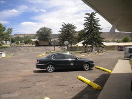 Um estacionamento com um carro preto estacionado perto de um edifício com um cesto de basquete.