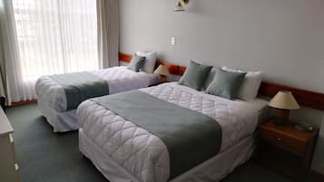 Quarto de hotel com duas camas, uma mesa de cabeceira com abajur e uma janela com cortinas.