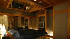 Um quarto tradicional em estilo japonês com tatames, uma cama com colcha azul-escuro, uma televisão sobre suporte de madeira e portas corrediças shoji.