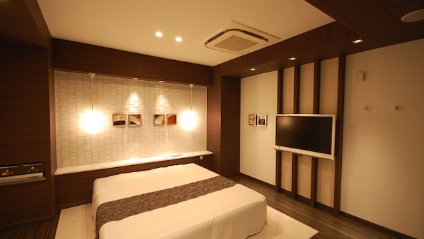 Quarto de hotel com uma cama grande, televisão e luminária fixada na parede.