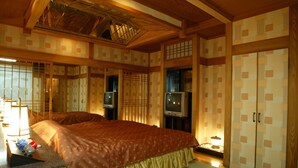 Quarto tradicional japonês com tatames, uma cama grande com colcha vermelha, duas televisões e portas deslizantes.