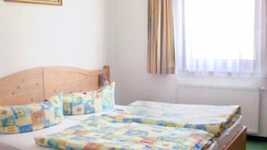 Quarto com cabeceira de madeira, cama com colcha estampada e janela com cortinas.
