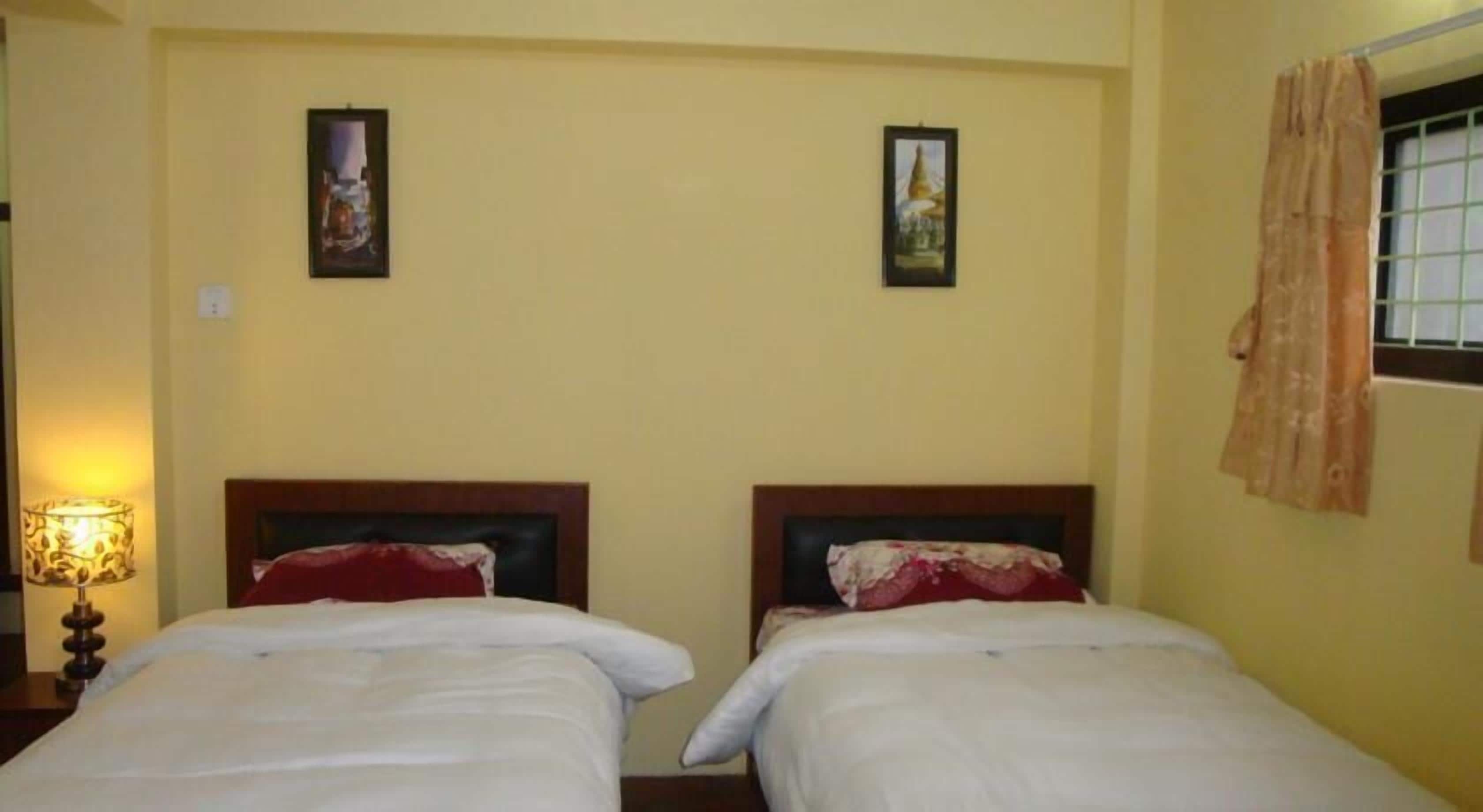 Quarto com duas camas de solteiro, uma luminária e duas fotos emolduradas na parede.