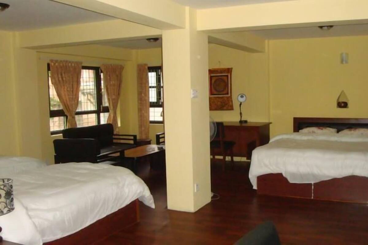 Quarto de hotel com duas camas, uma escrivaninha, uma cadeira e uma janela com cortinas.