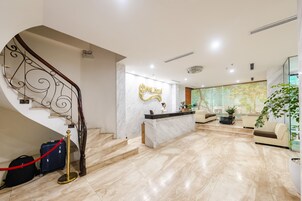 Um hall de hotel com escadaria de mármore, balcão de recepção e área de estar.