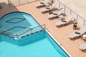 Piscina com escadas revestidas em azulejo e espreguiçadeiras com guarda-sóis.