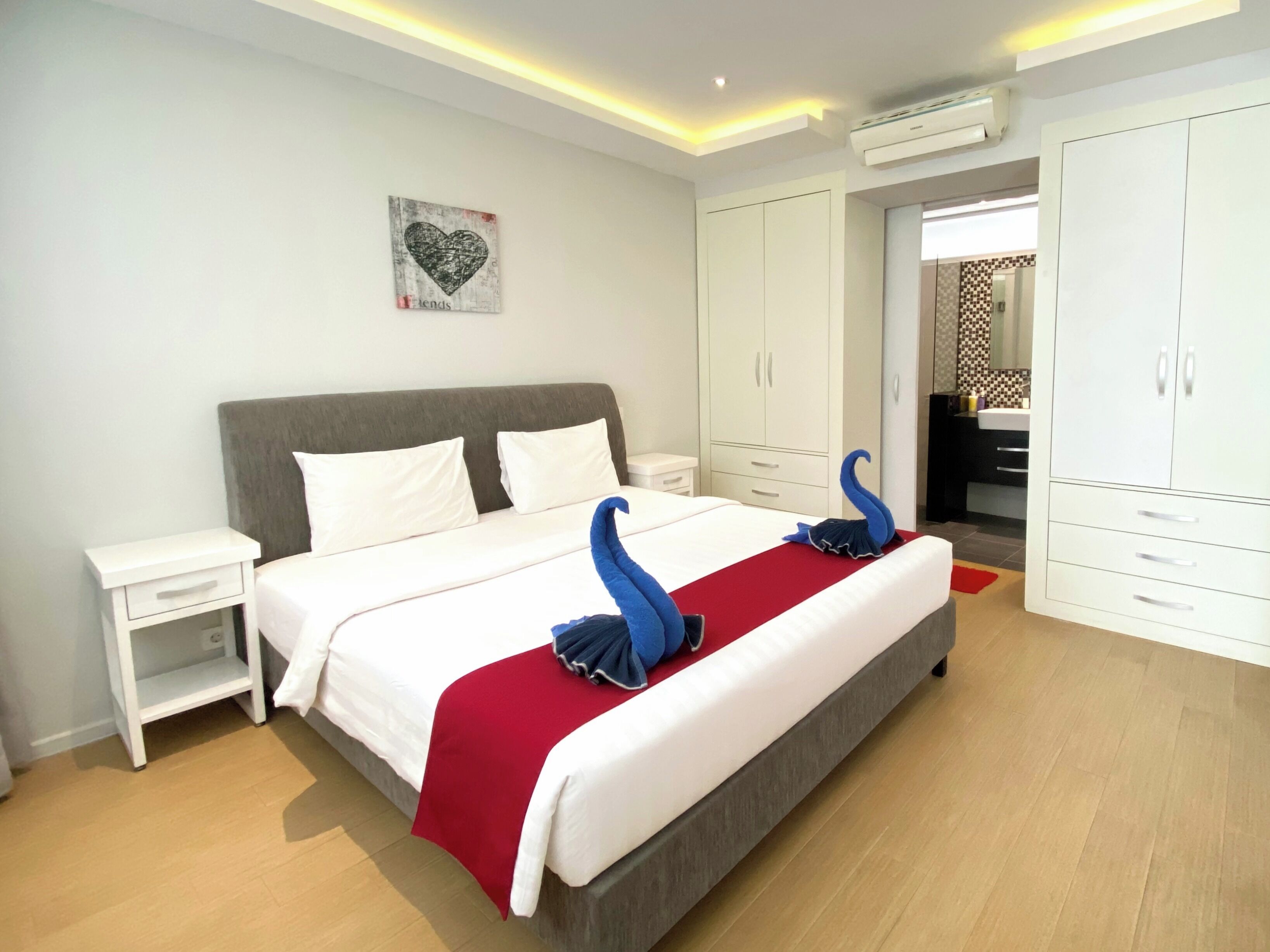 Um quarto moderno com uma cama grande, mesas de cabeceira brancas, um guarda-roupa e um coração decorativo na parede.
