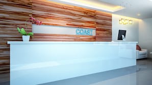 Um balcão de recepção moderno com painel de madeira ao fundo e a palavra 'COAST' escrita nele.