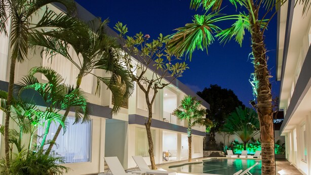 Uma área de piscina moderna ao ar livre, com espreguiçadeiras e palmeiras.